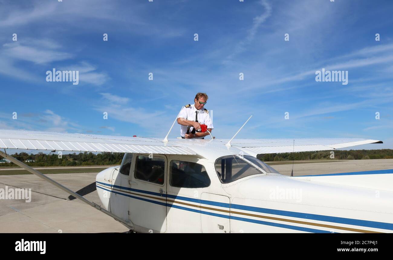 Young pilot filling up the airplane fuel tank on blue sky background ...