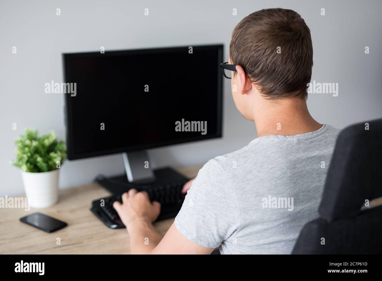 back view of young man using computer with blank screen at home or in ...
