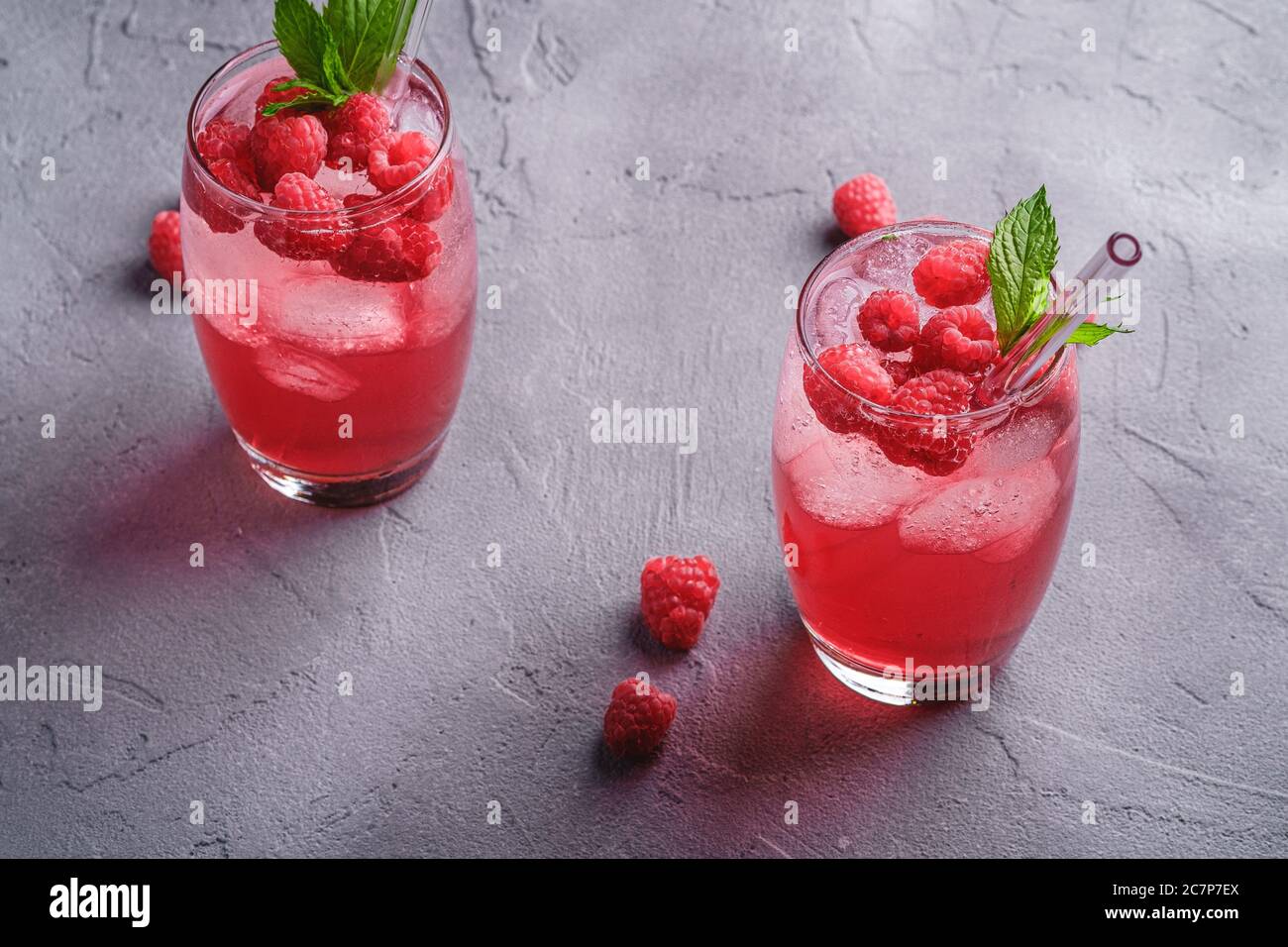 Fresh ice cold berry juice drink with mint, summer raspberry lemonade in two glass with straws ...