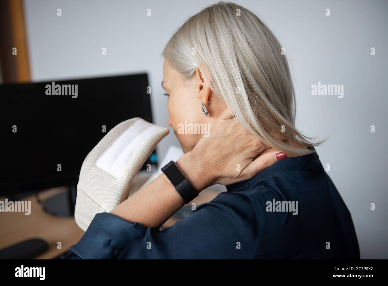Mature woman in pain wearing a surgical collar on her neck ,working on ...