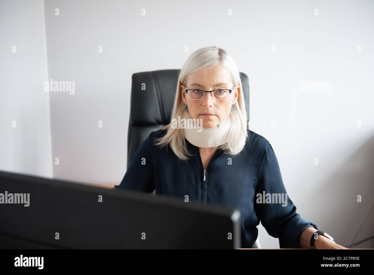 Mature woman in pain wearing a surgical collar on her neck ,working on ...