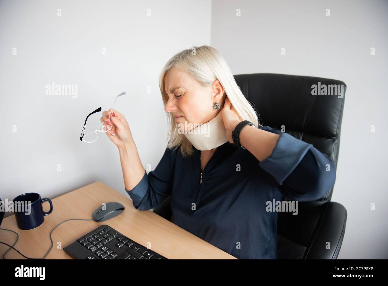 Mature woman in pain wearing a surgical collar on her neck ,working on ...