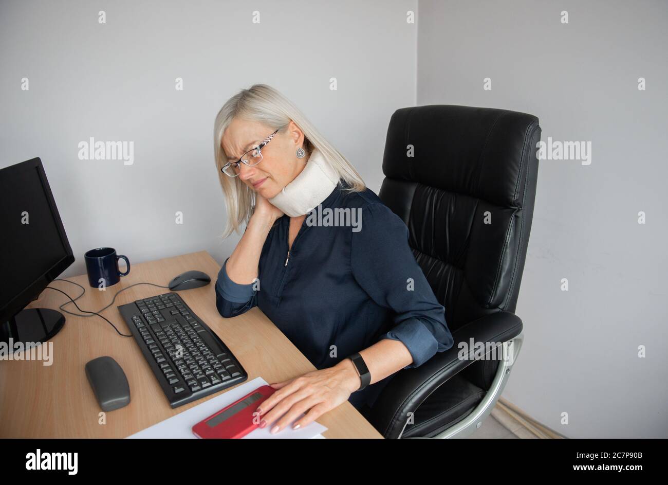 Mature woman in pain wearing a surgical collar on her neck ,working on ...