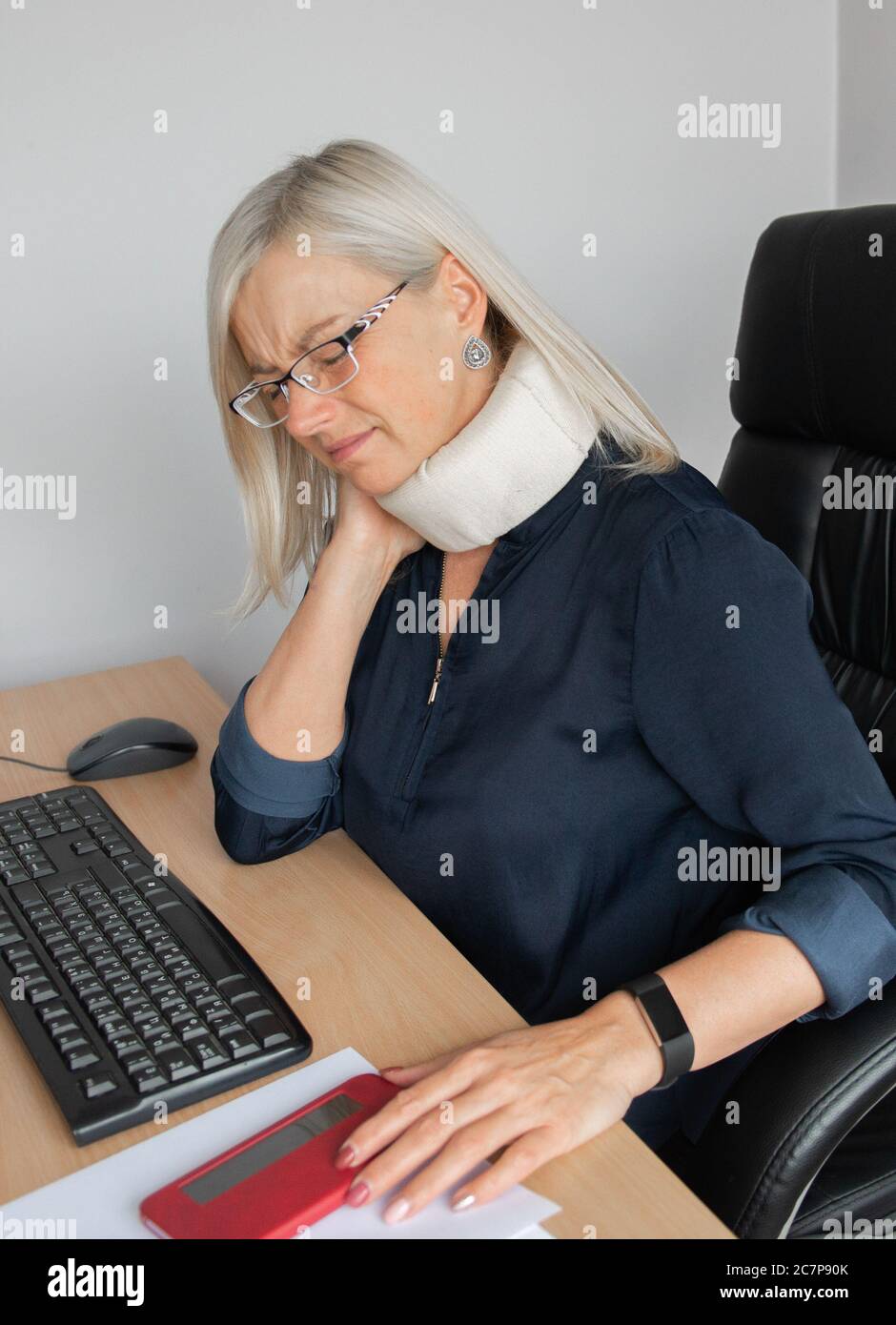 Mature woman in pain wearing a surgical collar on her neck ,working on ...