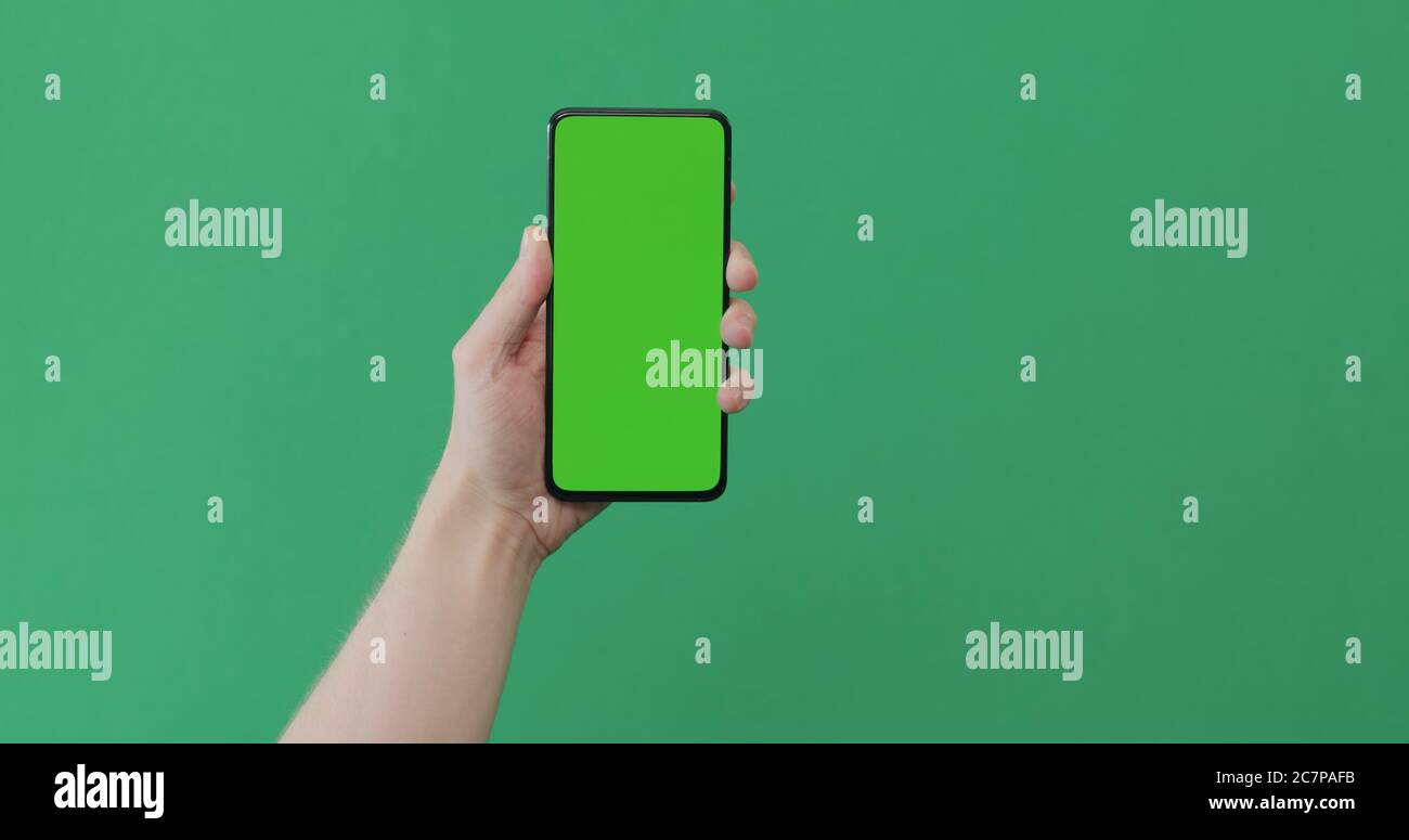 Young man hand hold smartphone with green screen on green background ...