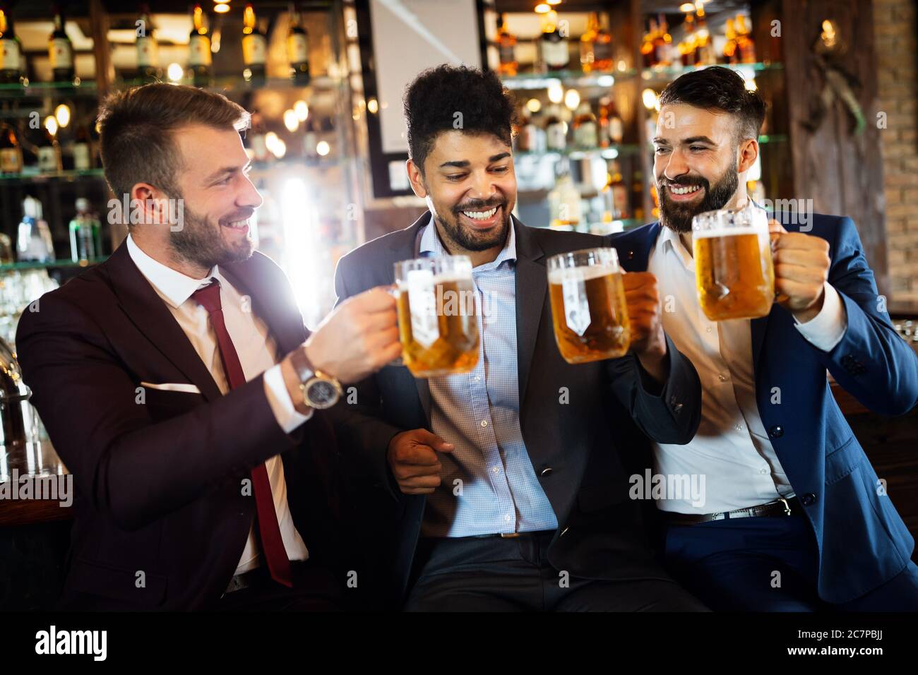 Happy young businessmen drinking beer and talking at pub after work ...