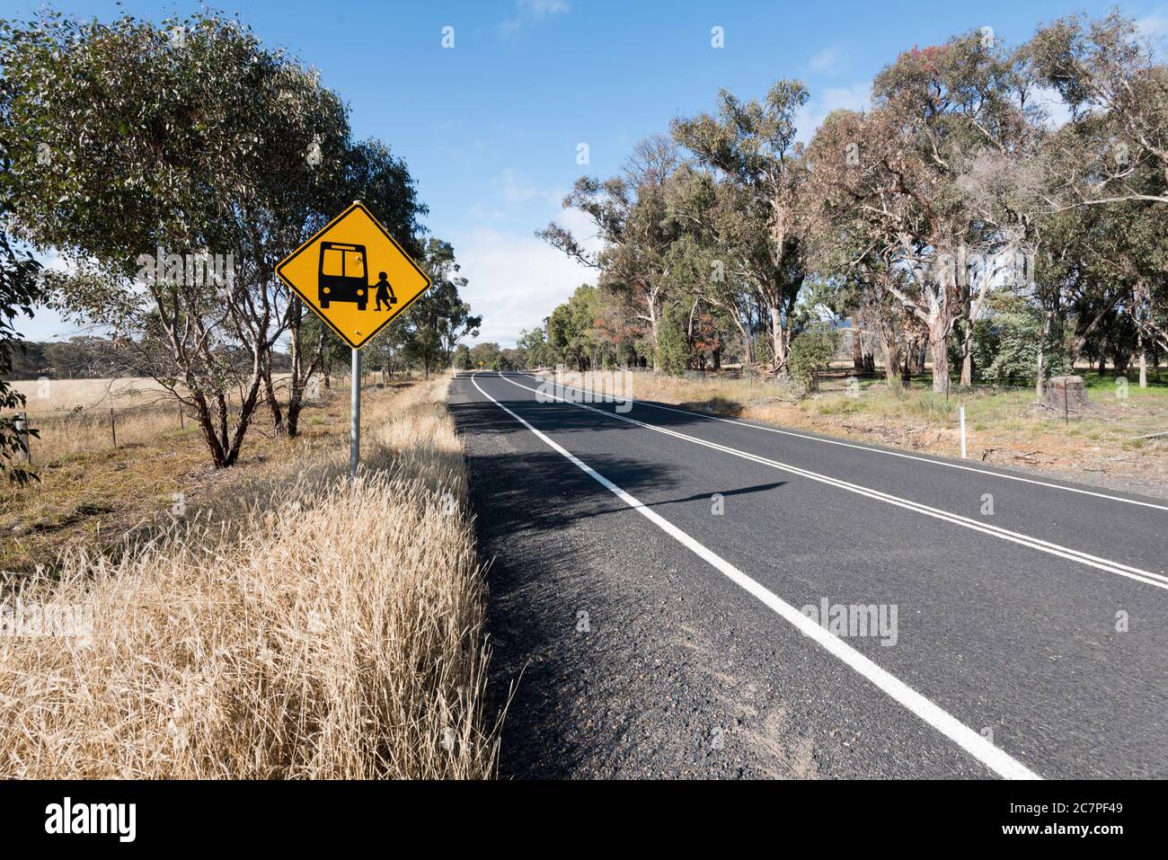 A country bus stop warning sign beside an empty long curved road near ...