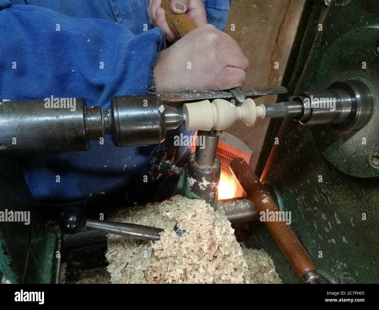 Man chiseling a wooden cylindrical block pinned in between of the shaft ...