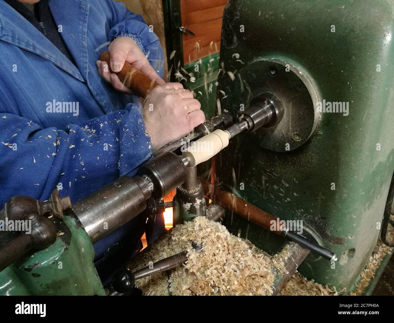 Man chiseling a wooden cylindrical block pinned in between of the shaft ...