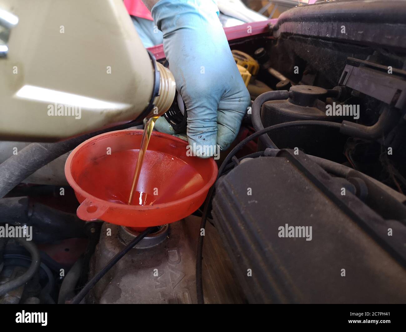 Man in gloves pouring lubrication oil in an engine using a funnel Stock ...