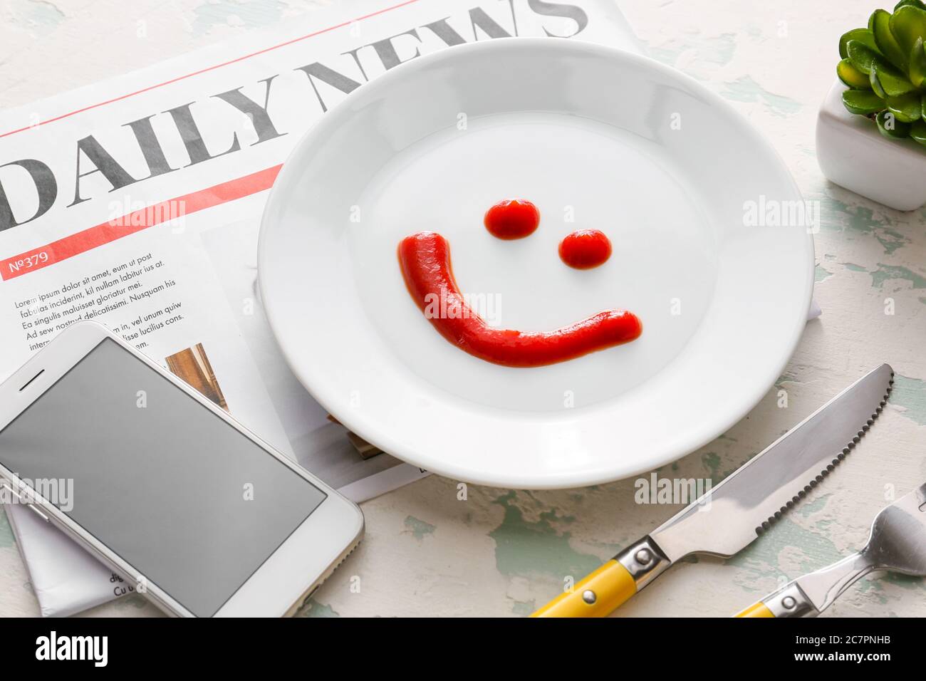 Happy face made of sauce on plate, cutlery, mobile phone and newspaper ...