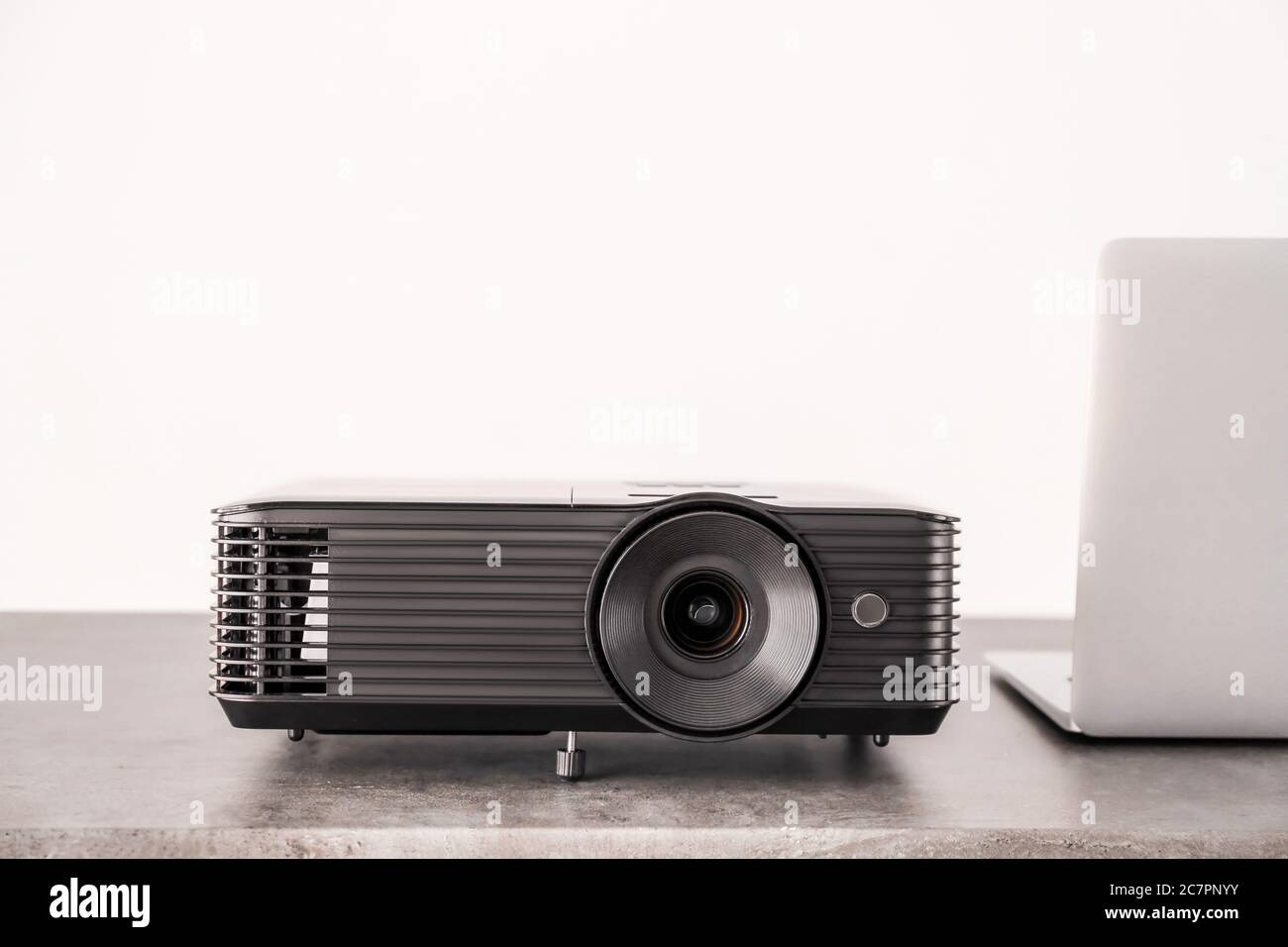 Modern video projector and laptop on table against white background ...