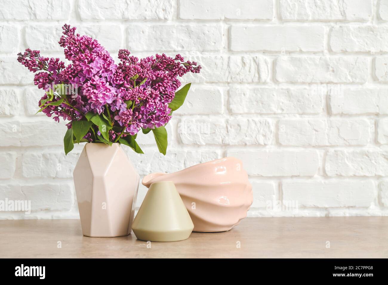 Vases with beautiful flowers on table near white brick wall Stock Photo ...