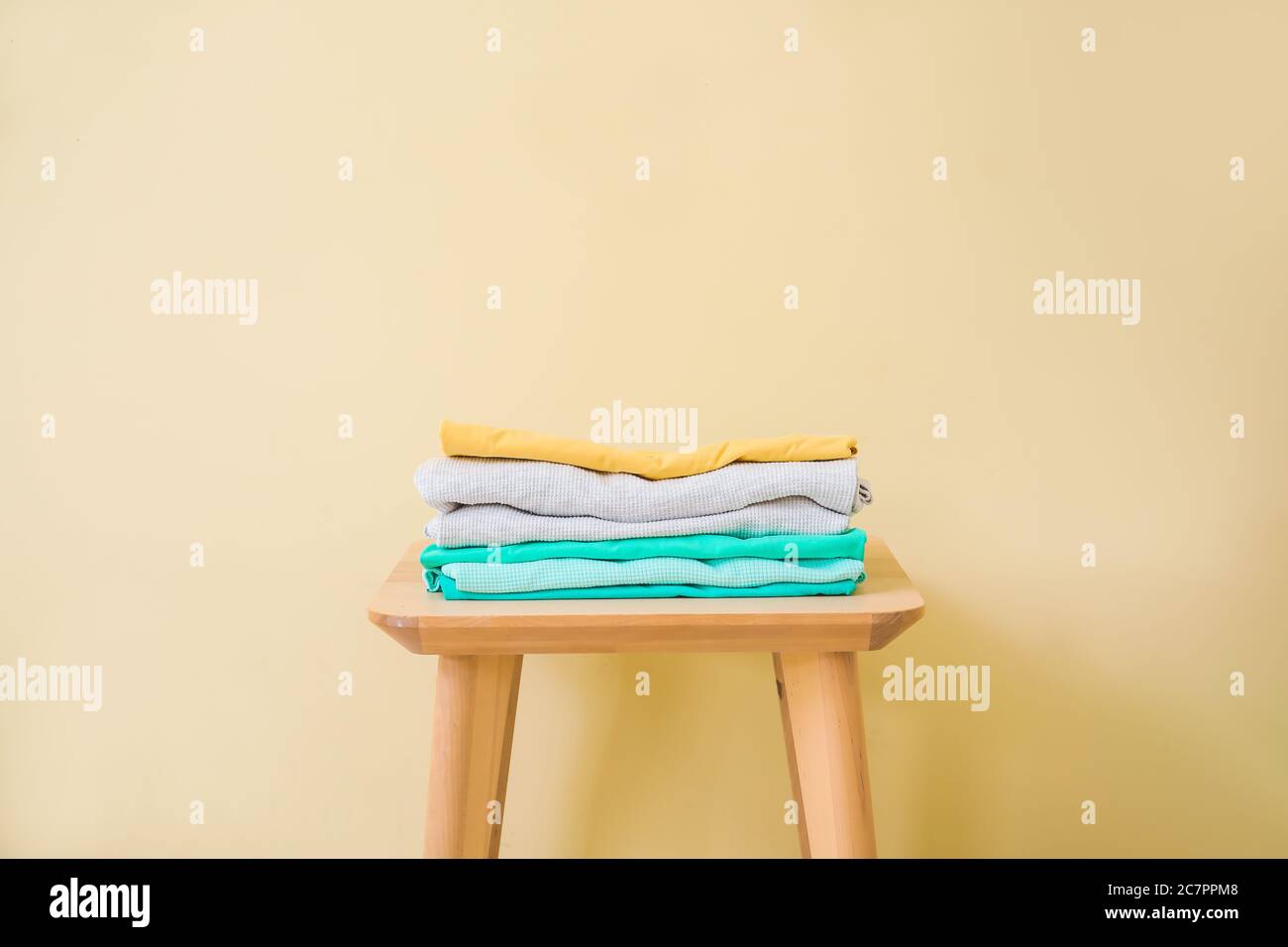 Stack of clean clothes on stool against color background Stock Photo ...