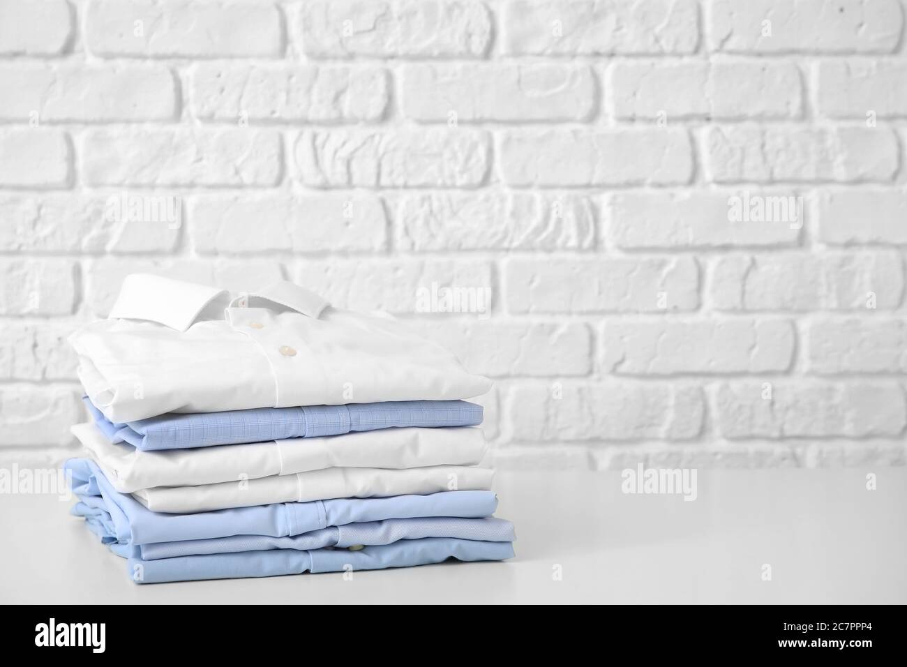 Stack of clean clothes on table against white brick background Stock ...