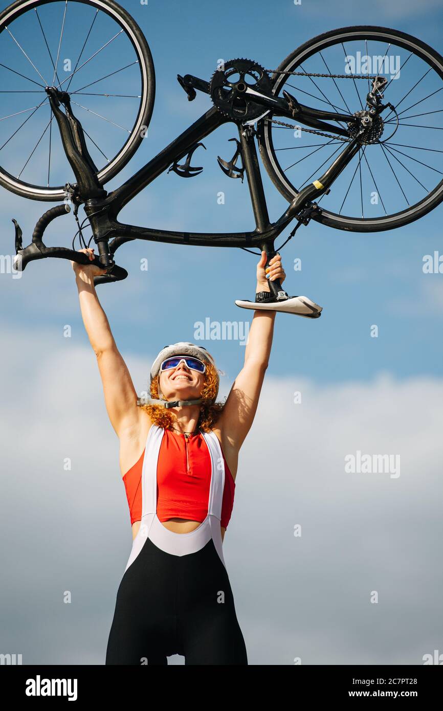 Strong victorious female athlete lifting bike over her head. Low angle ...