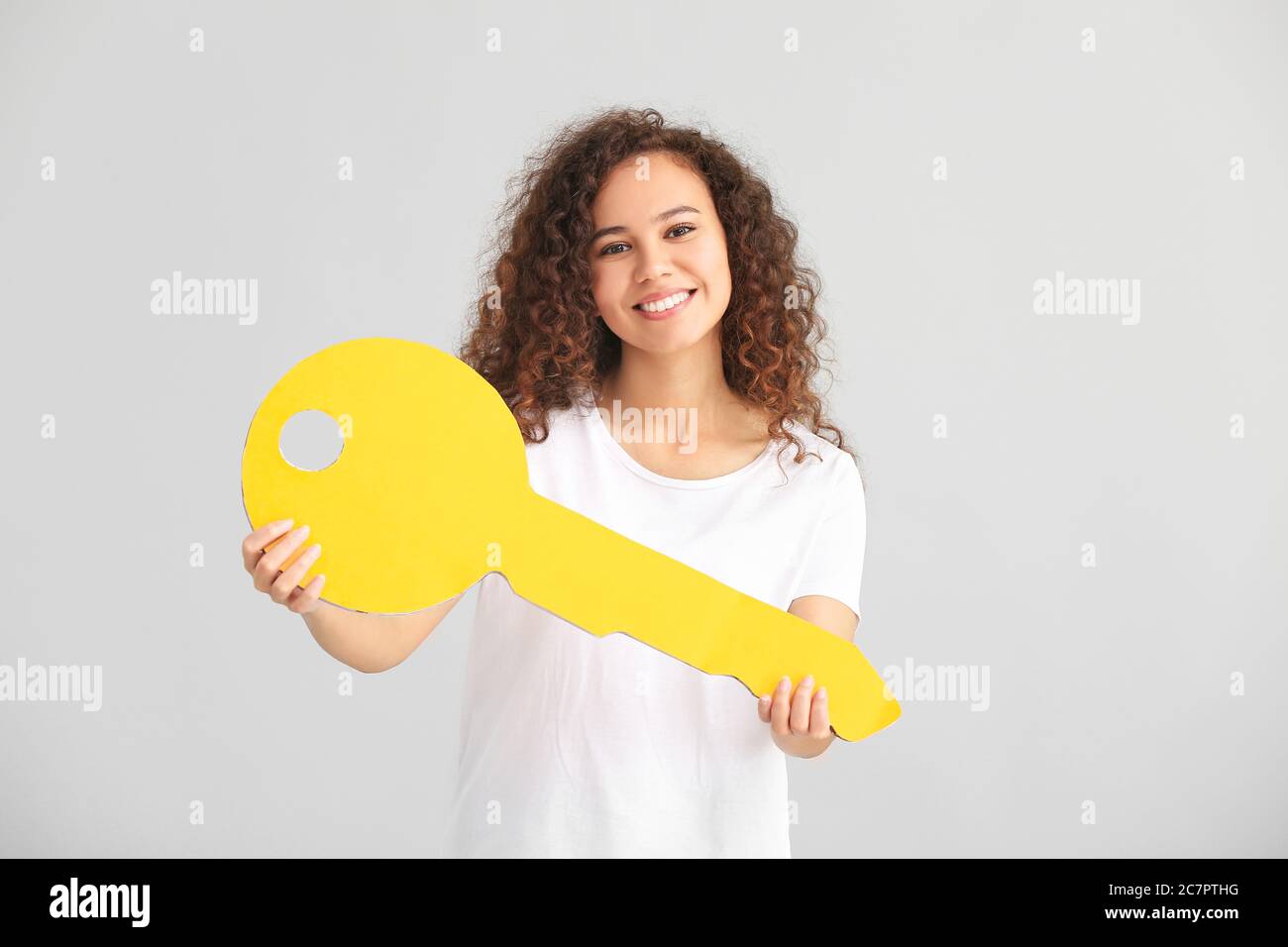 Young woman with big paper key on grey background Stock Photo - Alamy
