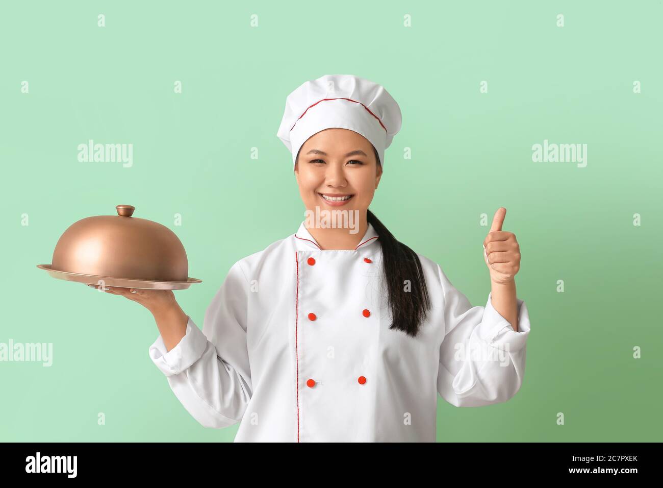Beautiful Asian chef with tray showing thumb-up gesture on color ...