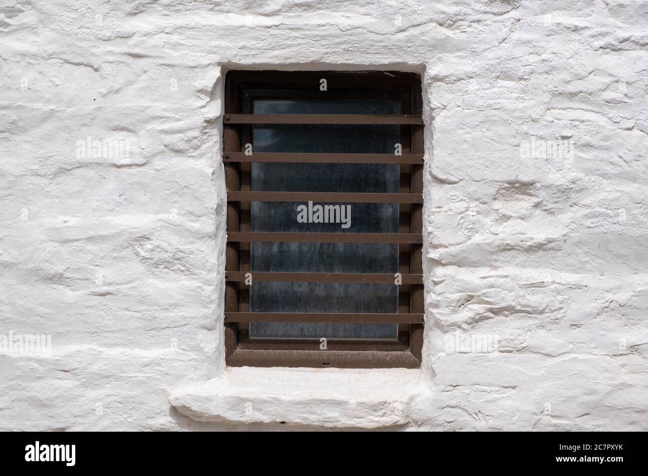 Brown color painted window with security bars on a white stone wall ...