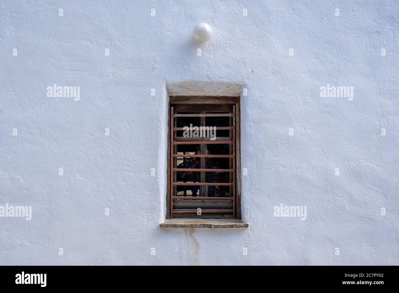 Brown color painted window with security bars on a white stone wall ...