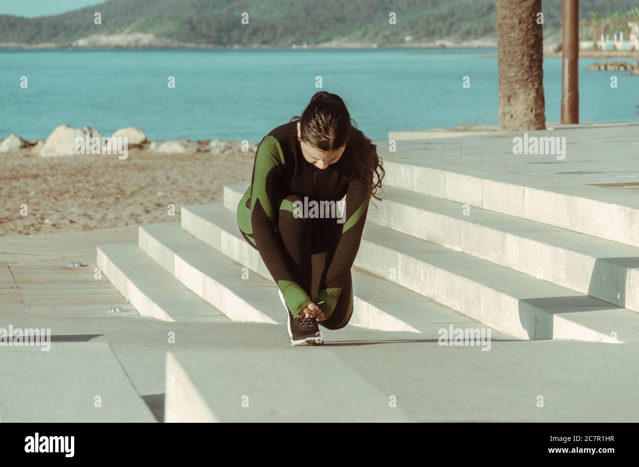 Young female tying her laces while working out surrounded by the sea ...