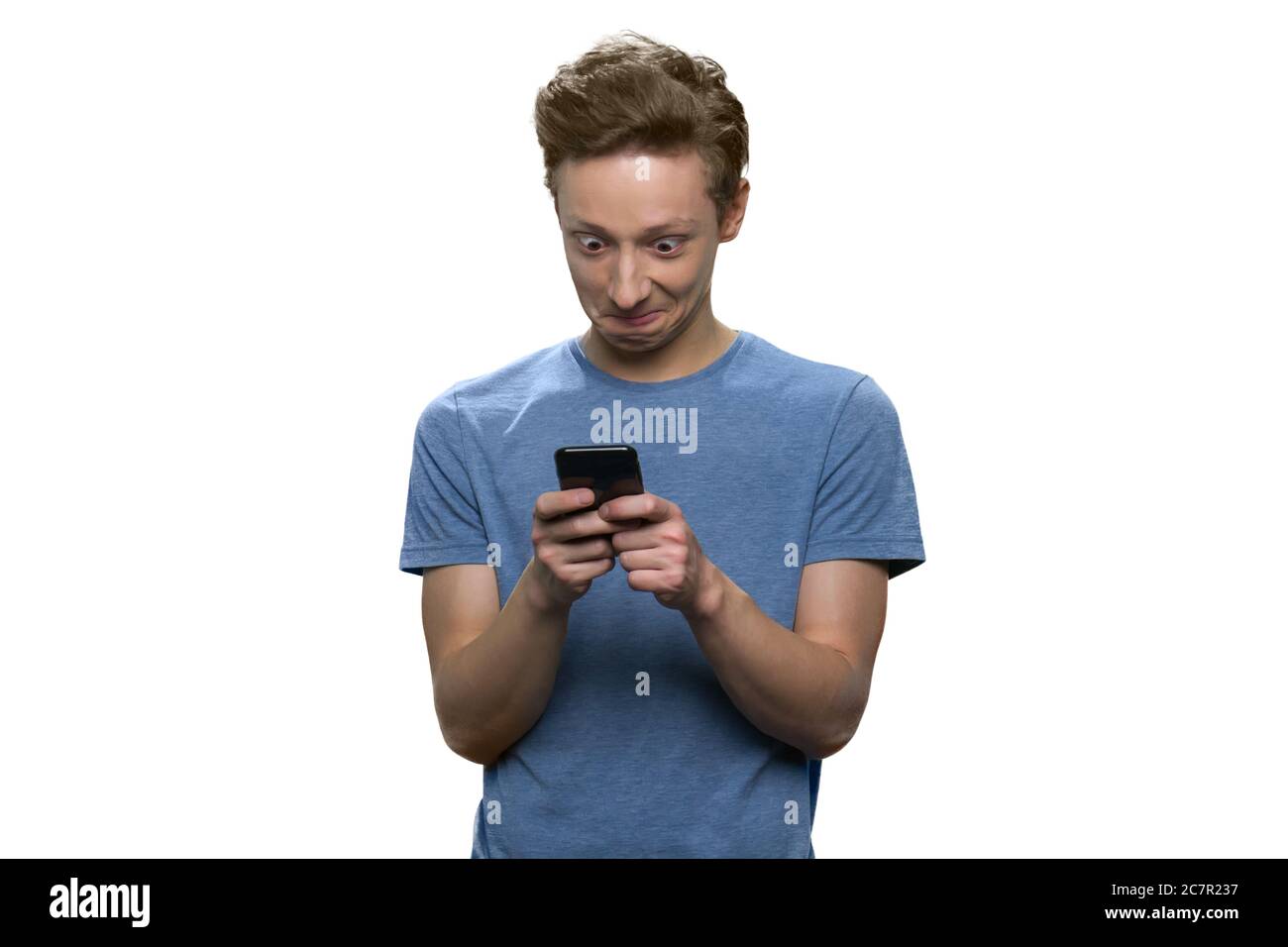 Surprised teenager with widely opened eyes is looking at his smartphone ...