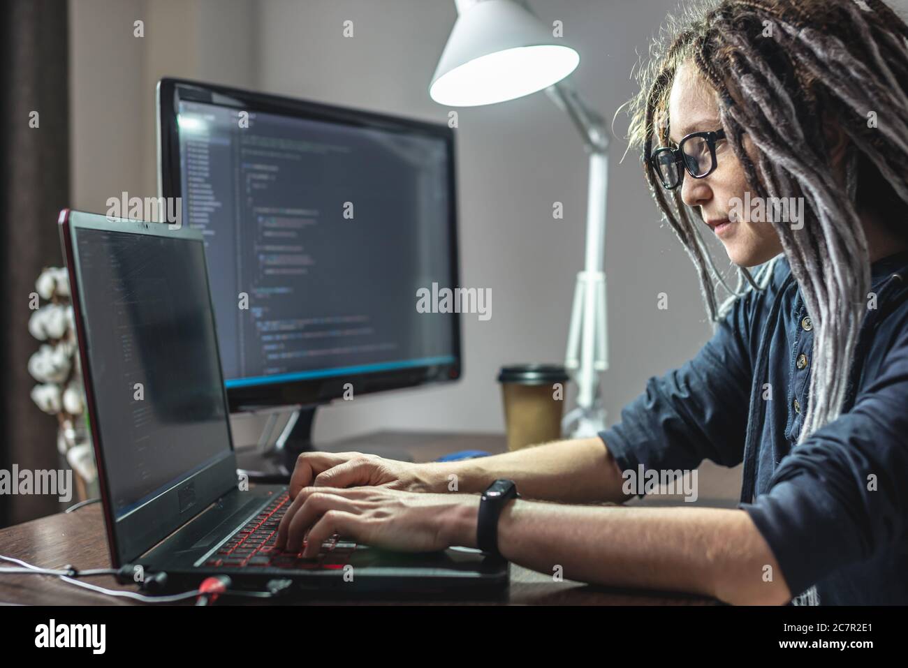 Modern young female programmer is writing program code on a laptop at home. Remote work in the ...