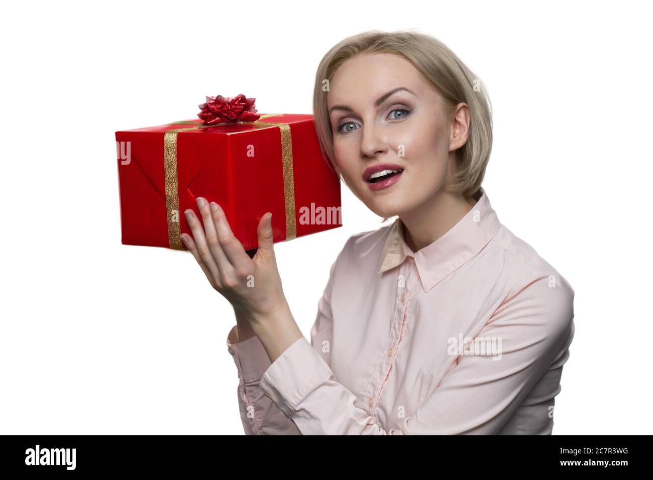 Curious young lady looking up and putting her ear to red gift box Stock ...