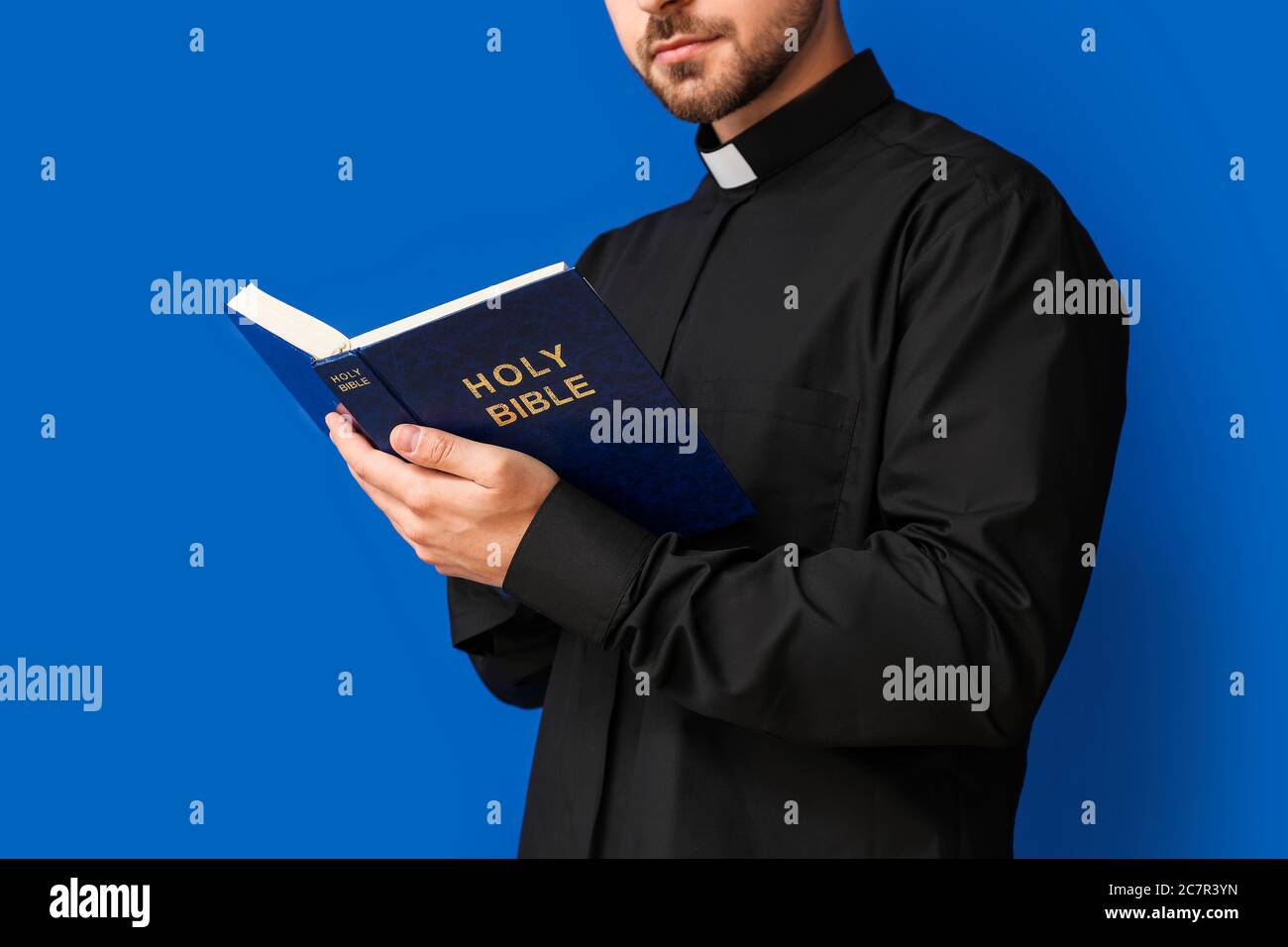 Young priest reading Bible on color background Stock Photo - Alamy
