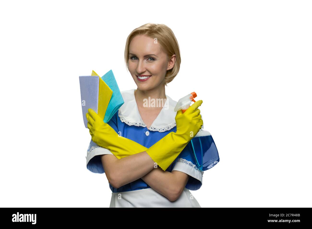 Young maid standing with arms crossed holding cleaning stuff on white ...