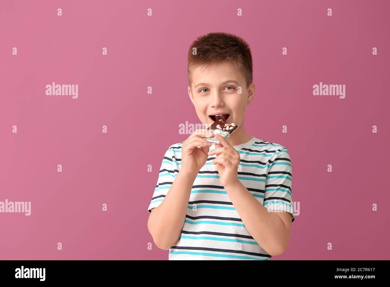 Cute little boy eating chocolate on color background Stock Photo - Alamy