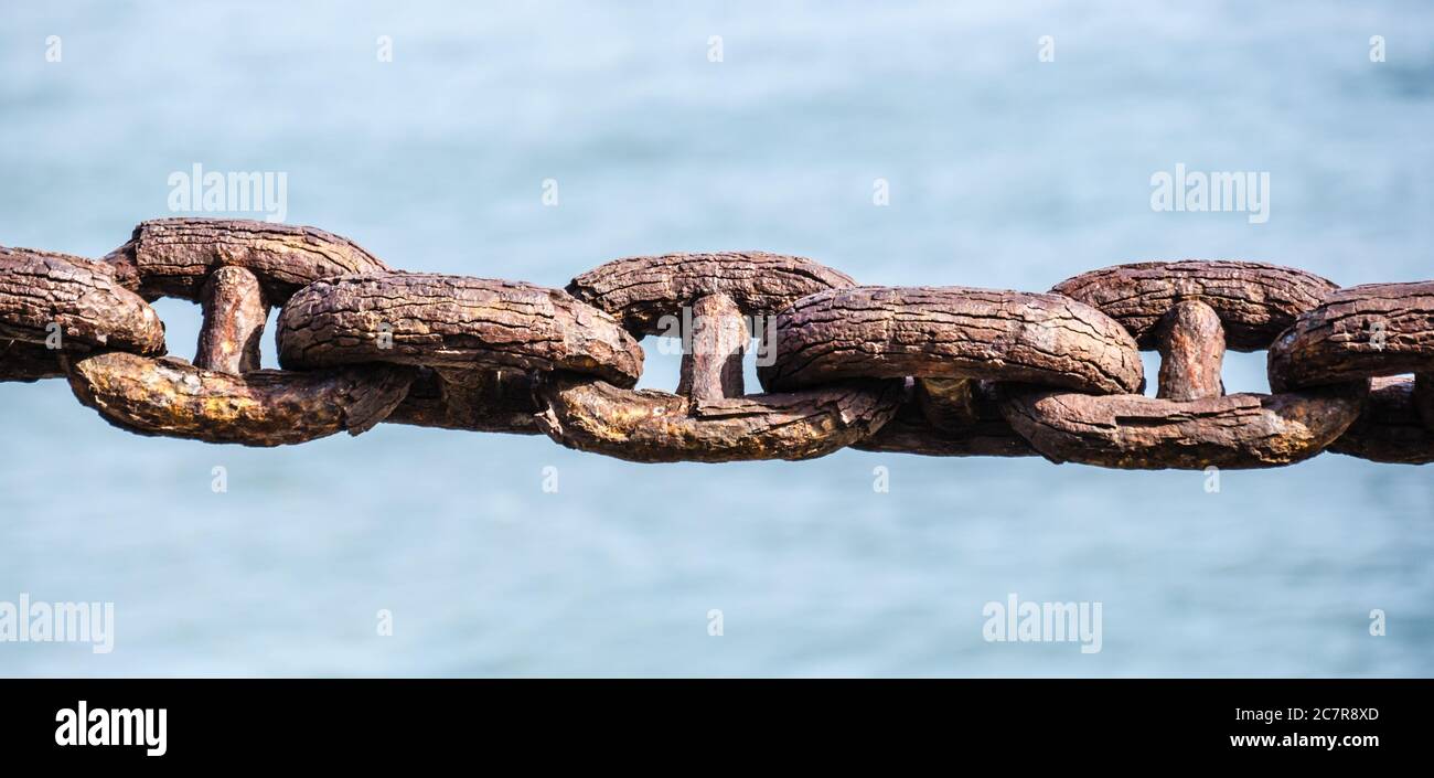 Closeup shot of a rusty old interlinked chain on a blue background ...