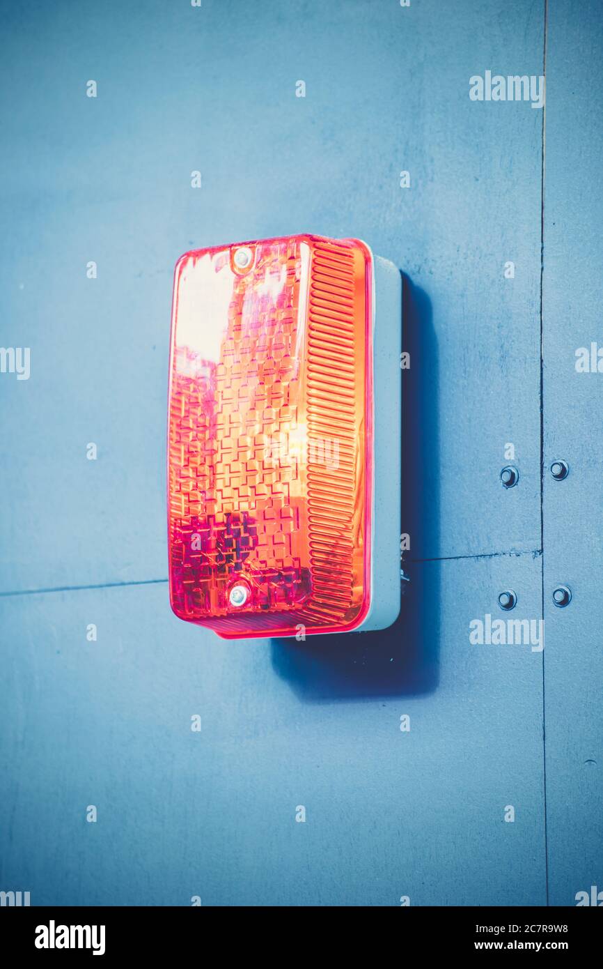 Vertical closeup shot of a red warning light hanging on a light blue ...