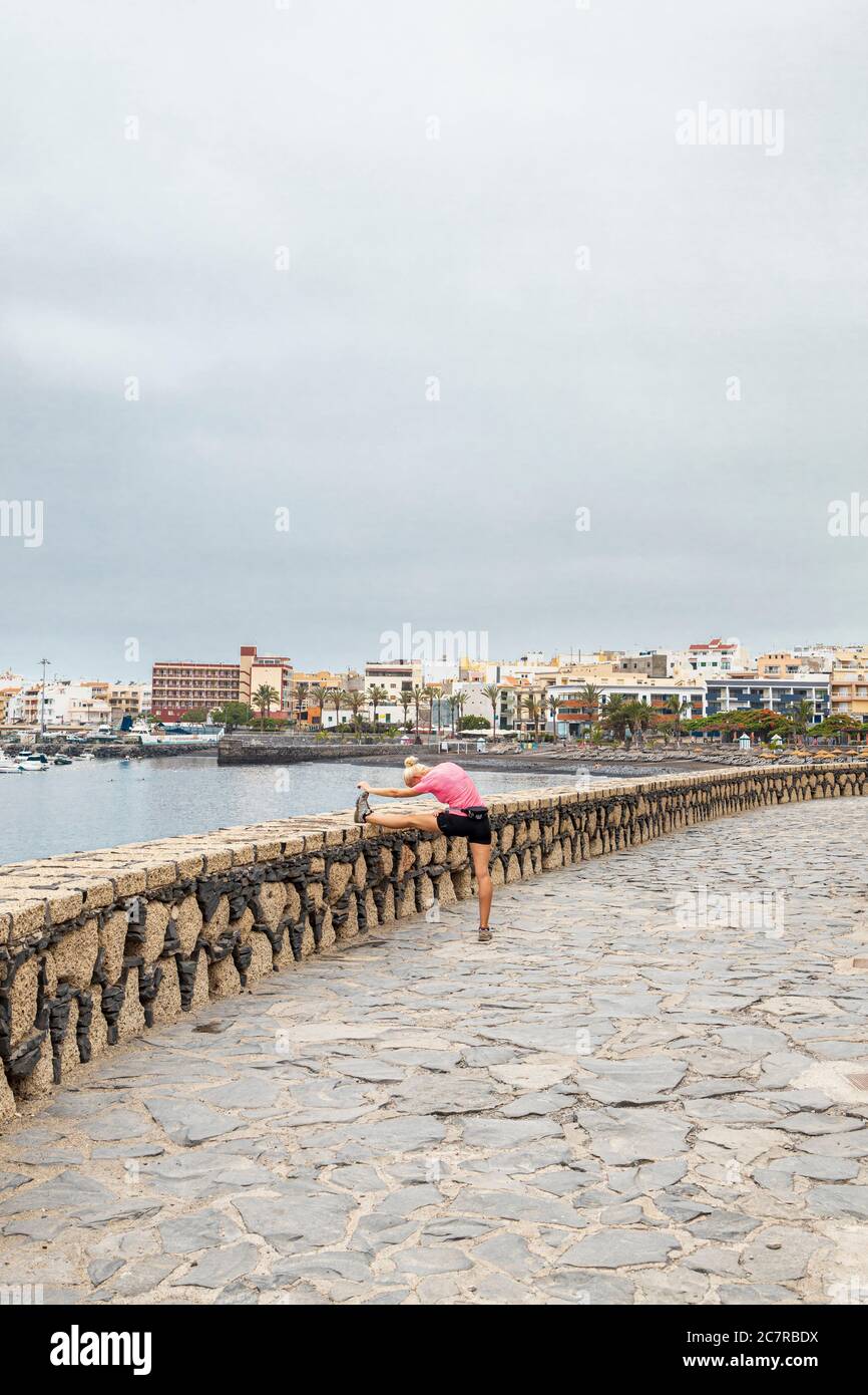 Woman stretching her leg muscles on the wall along the promenade at ...
