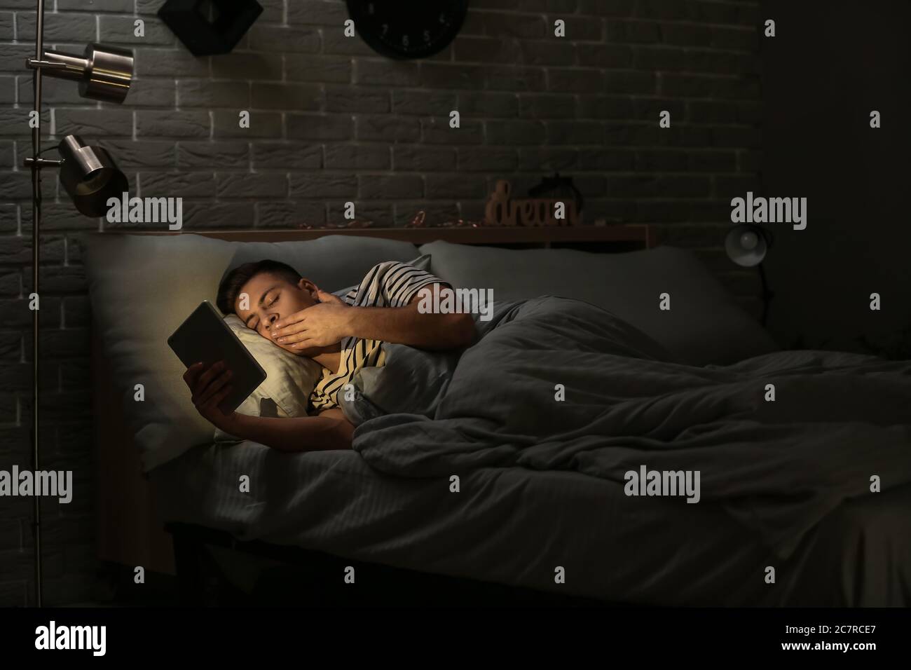 Young man suffering from sleep deprivation with tablet computer in ...