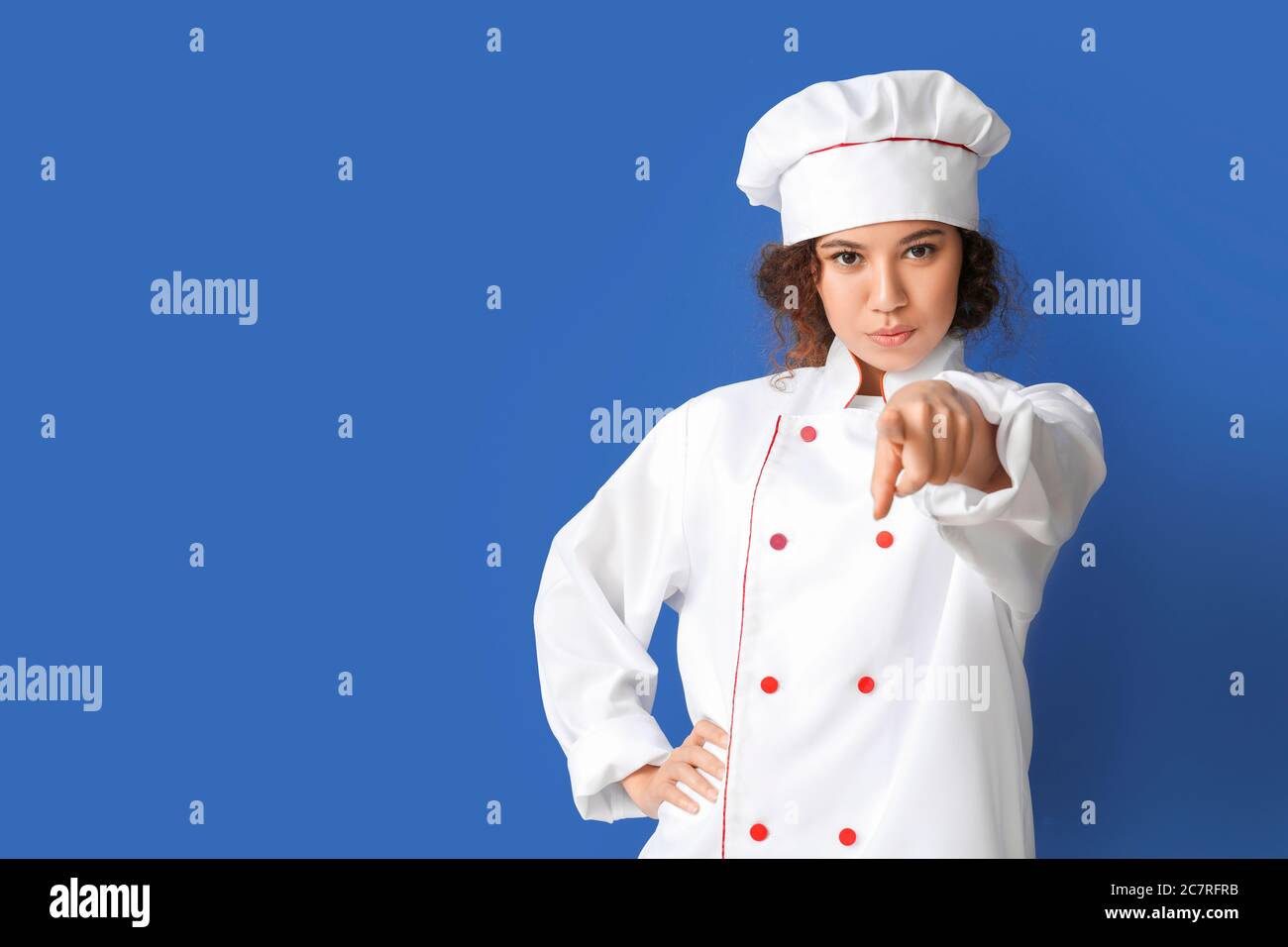 Female African-American chef pointing at viewer on color background ...