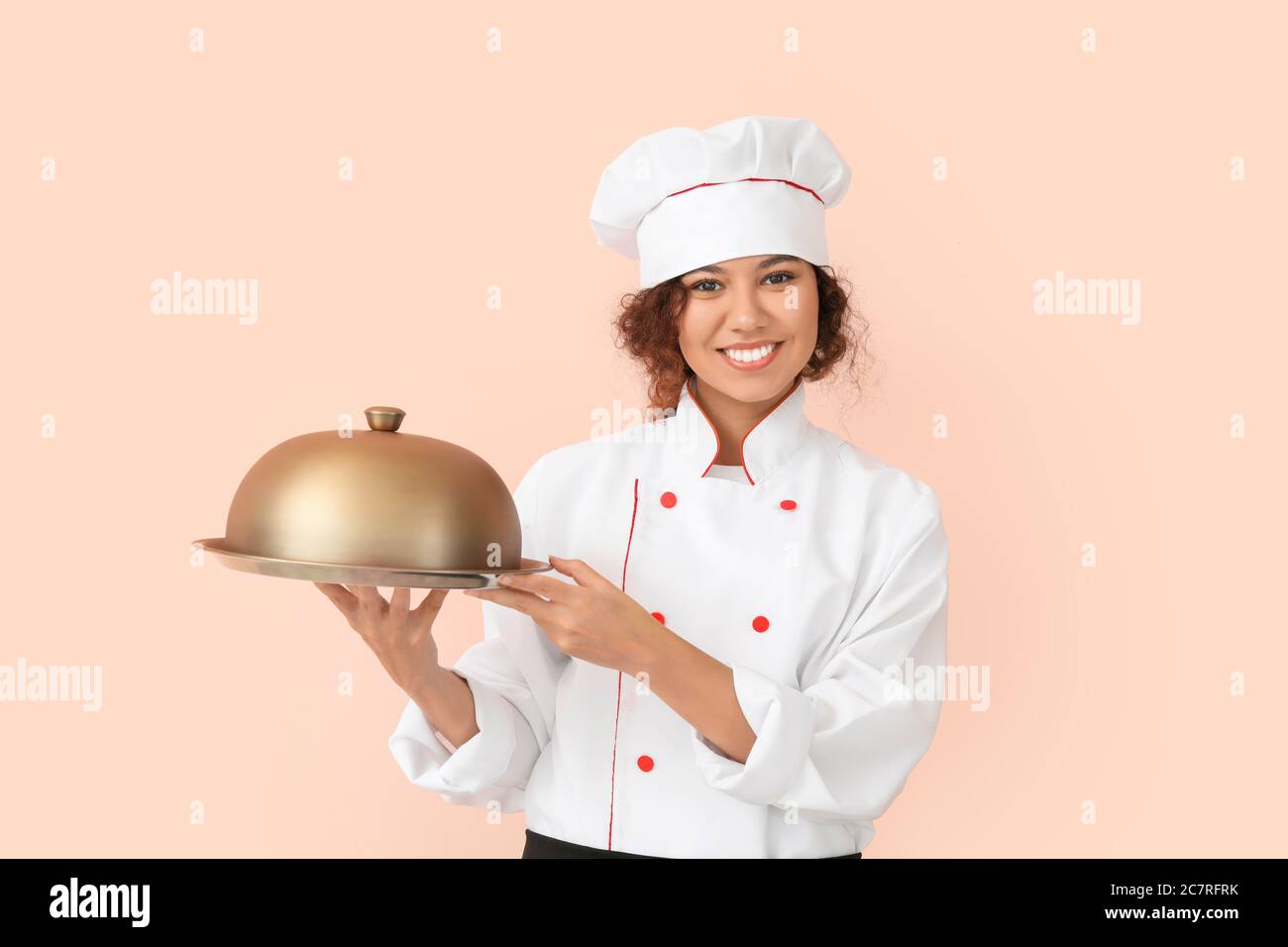 Female African-American chef with tray and cloche on color background ...