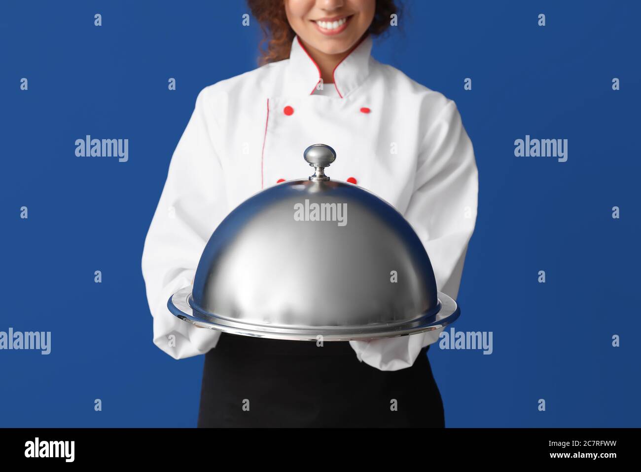 Female African-American chef with tray and cloche on color background ...