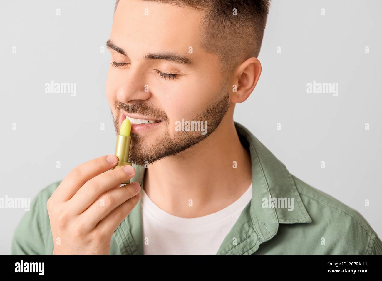 Handsome young man with lip balm on light background Stock Photo - Alamy