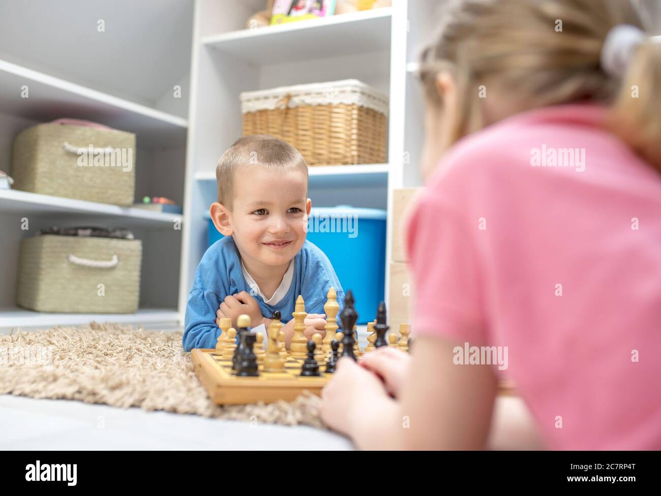 Adorable siblings lying on the ground and playing chess with each other ...