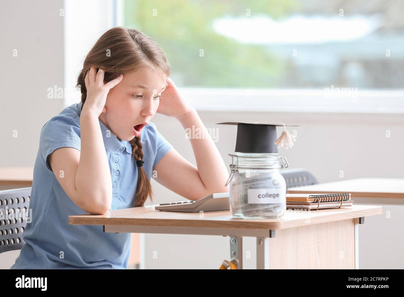 Shocked girl with savings for education and calculator in classroom ...
