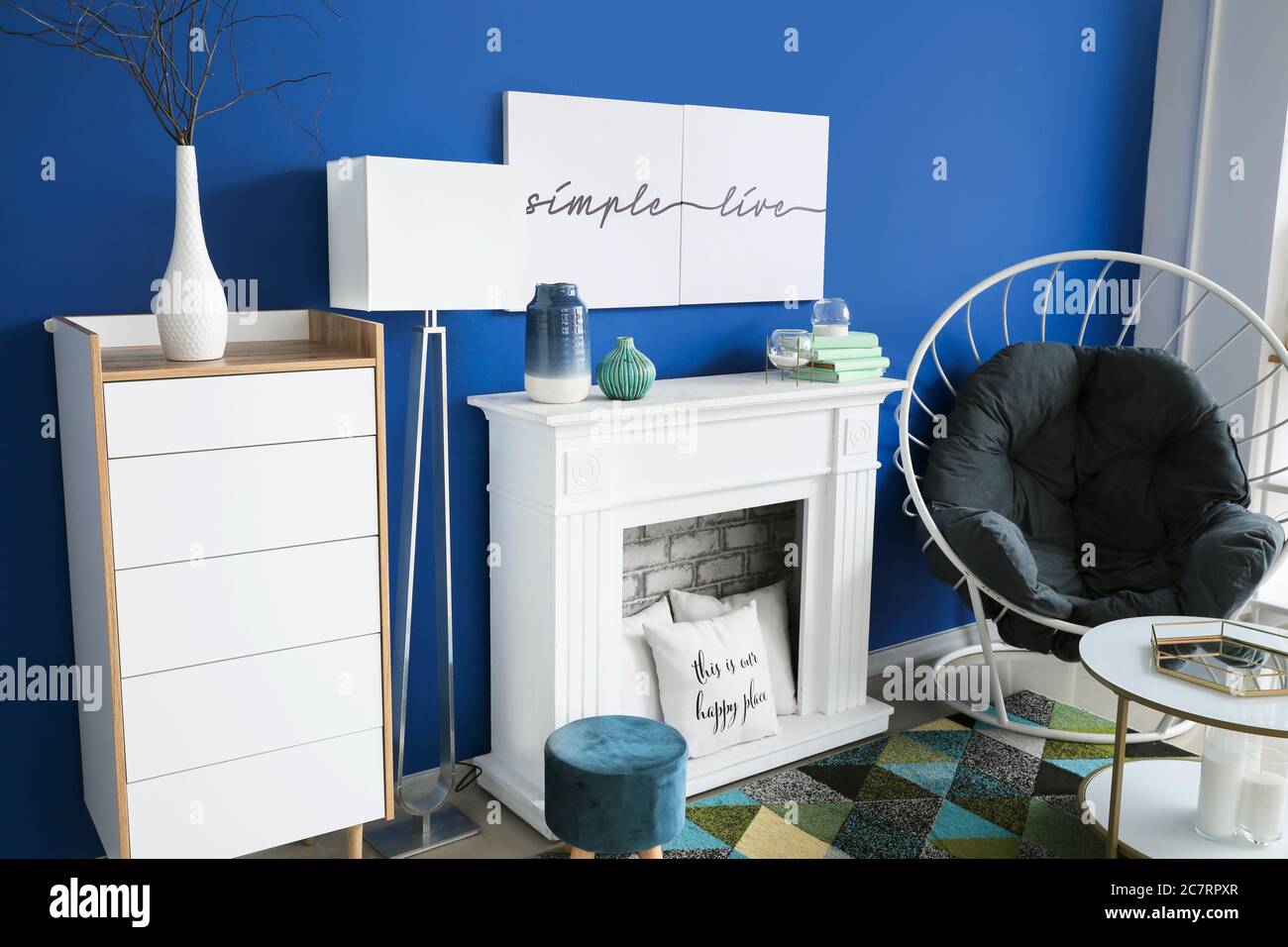 Stylish fireplace with armchair and chest of drawers in interior of ...