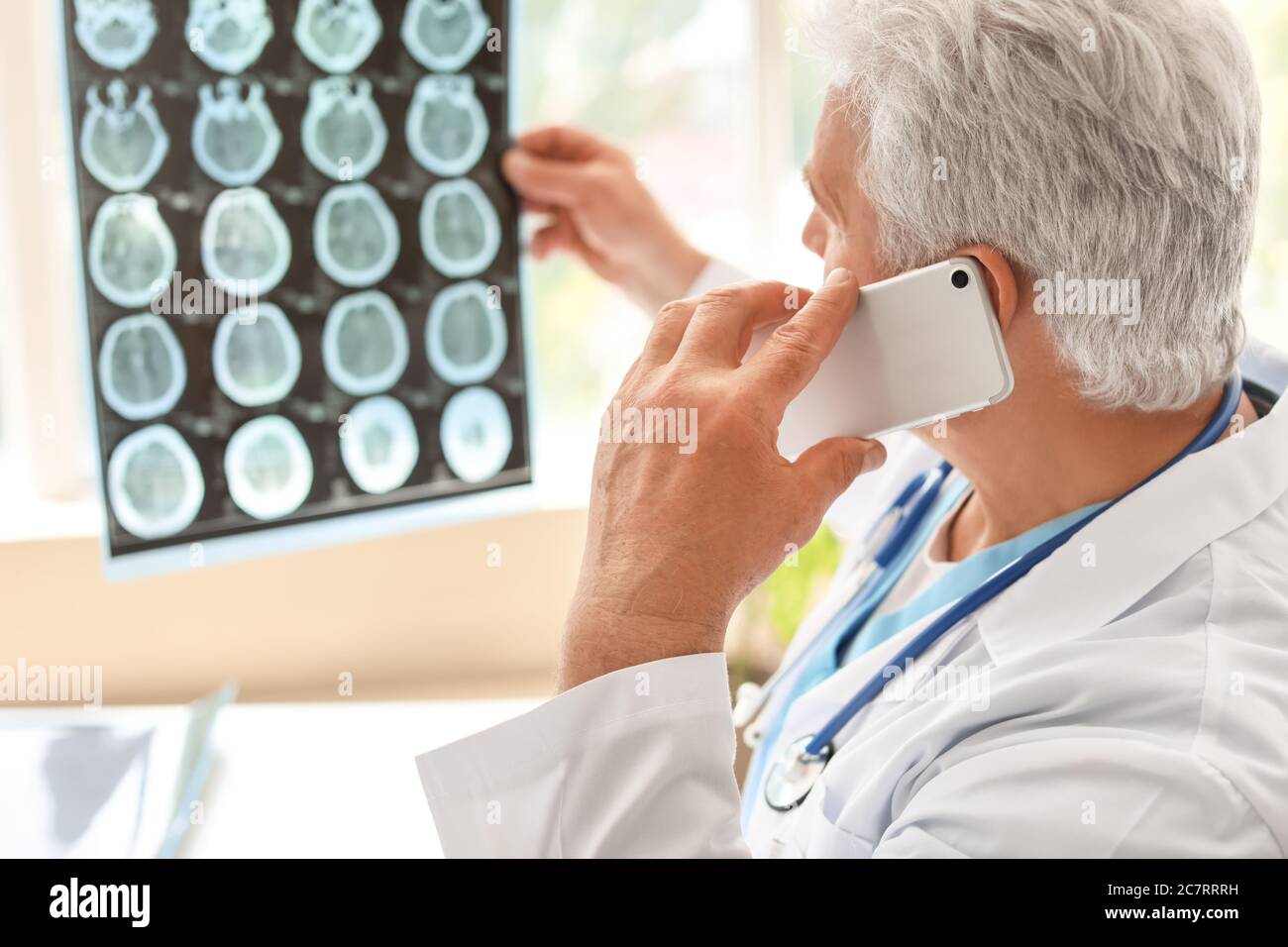 Senior neurologist with MRI scan of human head talking by mobile phone ...
