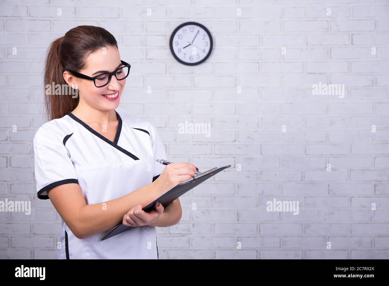 young beautiful woman doctor writing something on clipboard over white ...