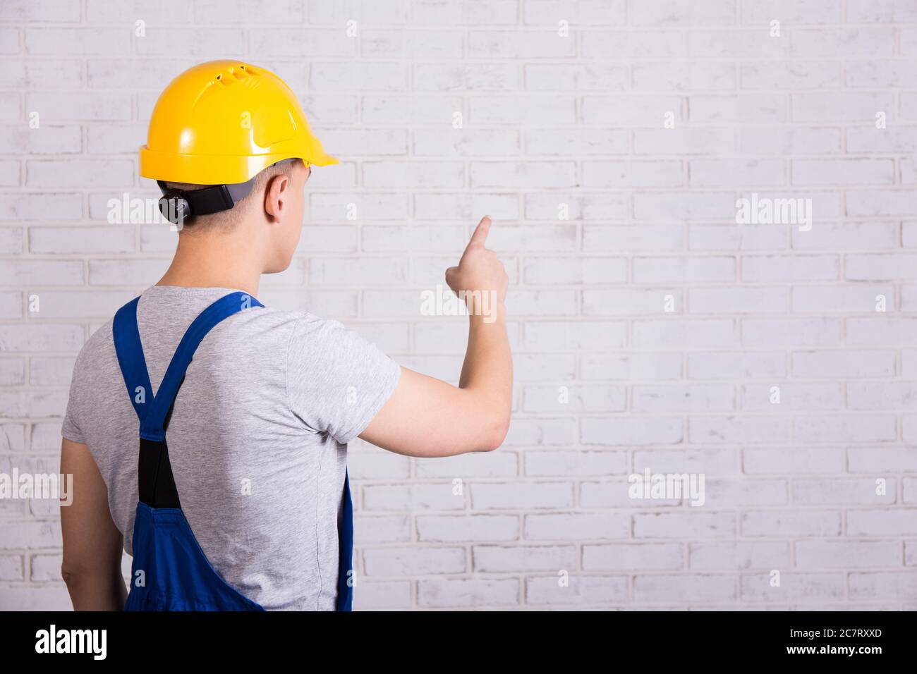 back view of man in blue builder uniform pointing at white brick wall ...
