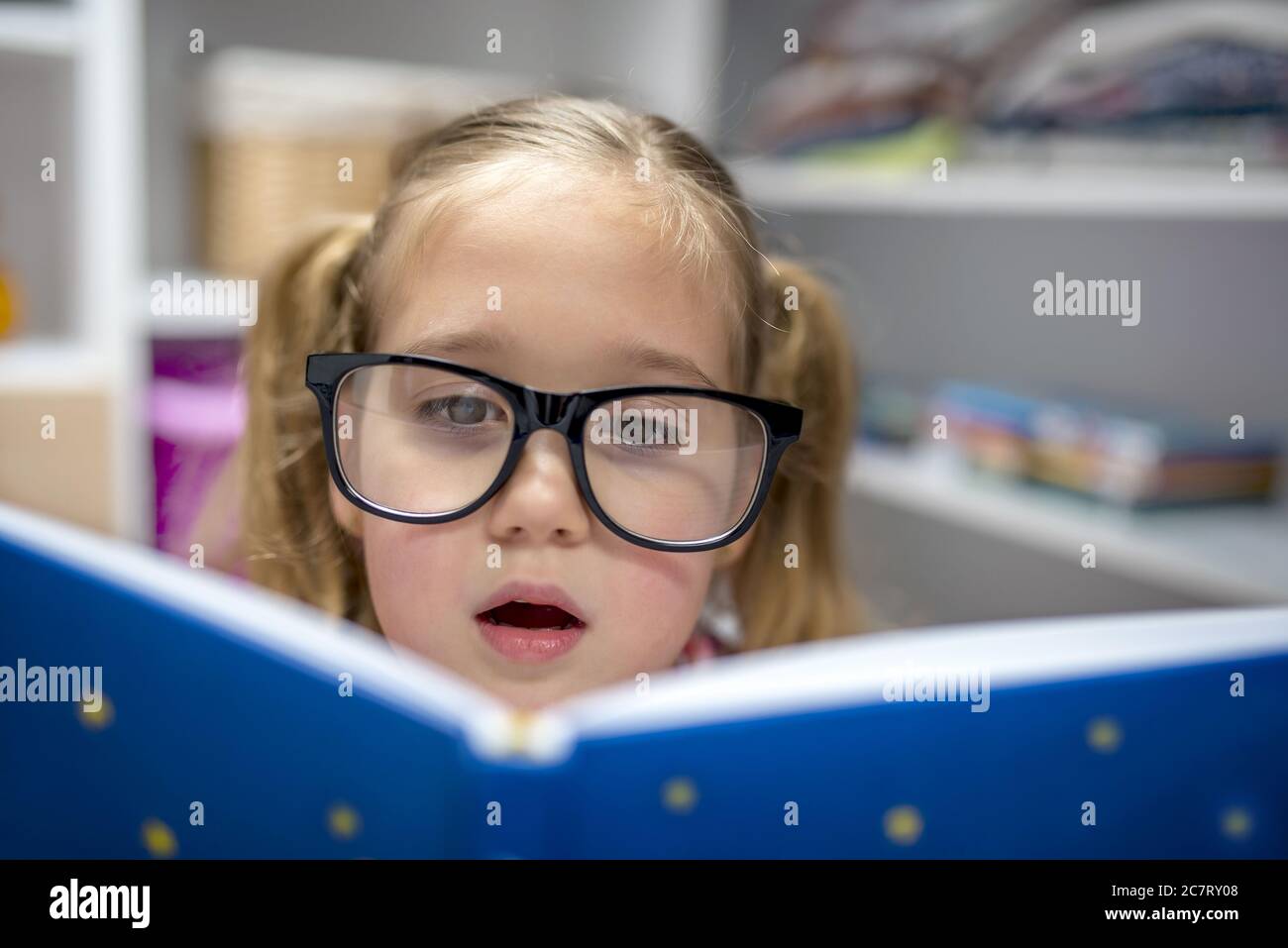 Adorable little girl with glasses reading a book with a surprised ...