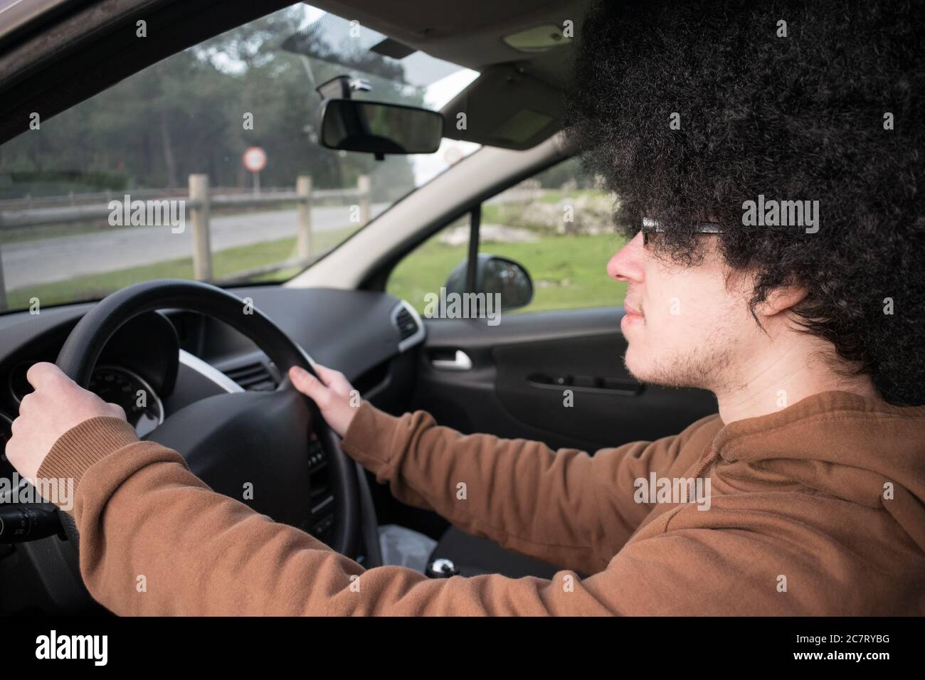African-American young male with curly hair driving a car at daytime ...