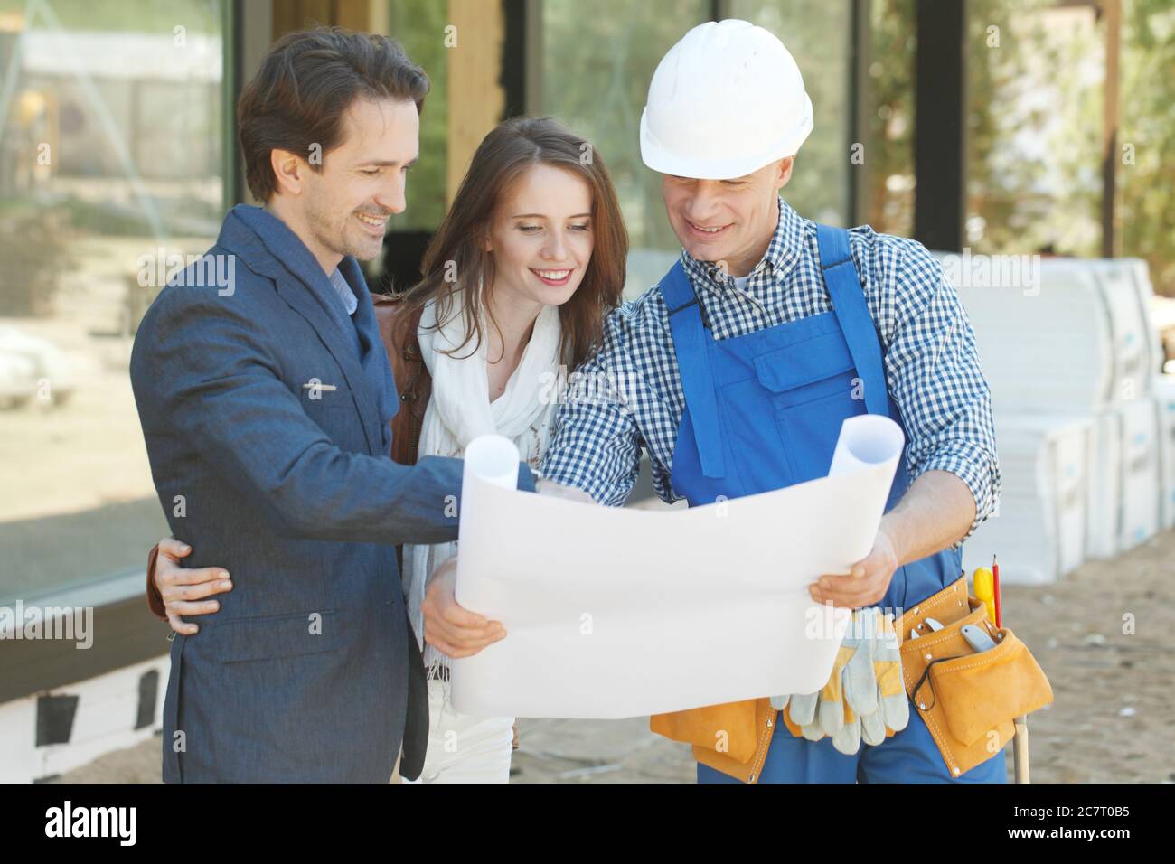 Foreman showing house design construction plan to a happy young couple ...