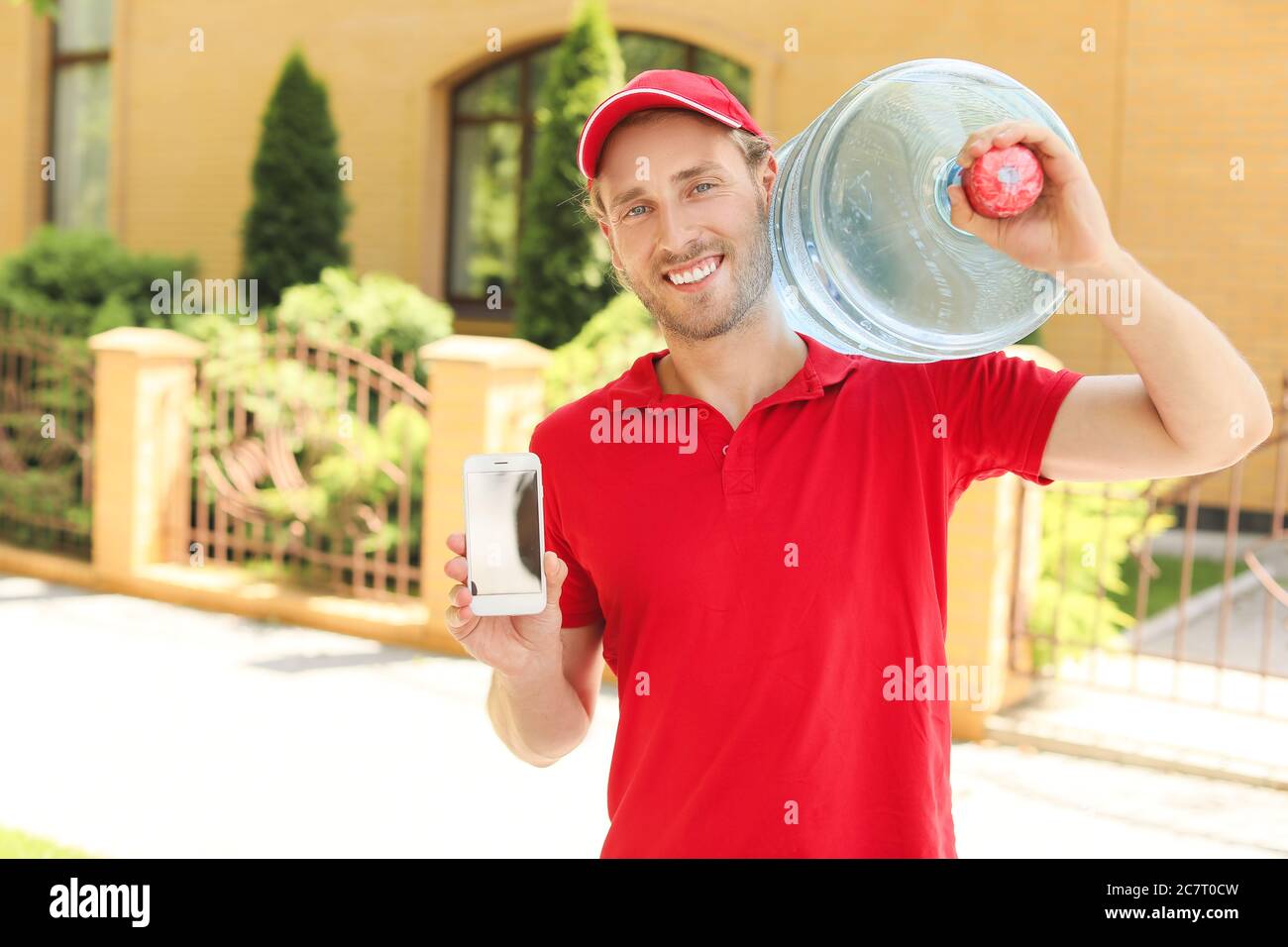 Delivery man with bottle of water and mobile phone outdoors Stock Photo ...