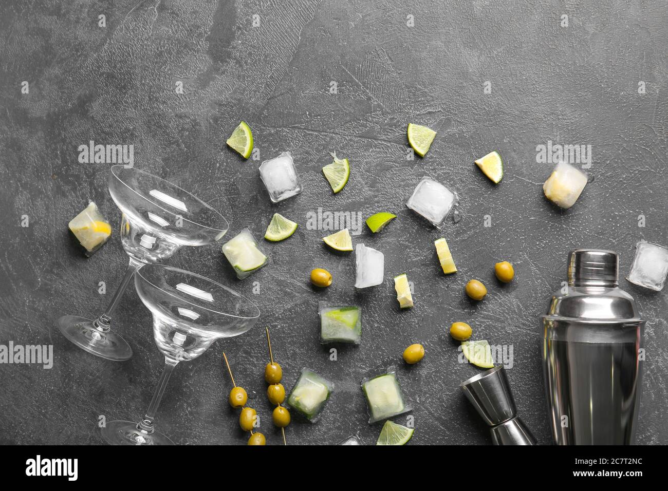 Cocktail glasses with shaker, ice cubes, olives and lime slices on dark ...